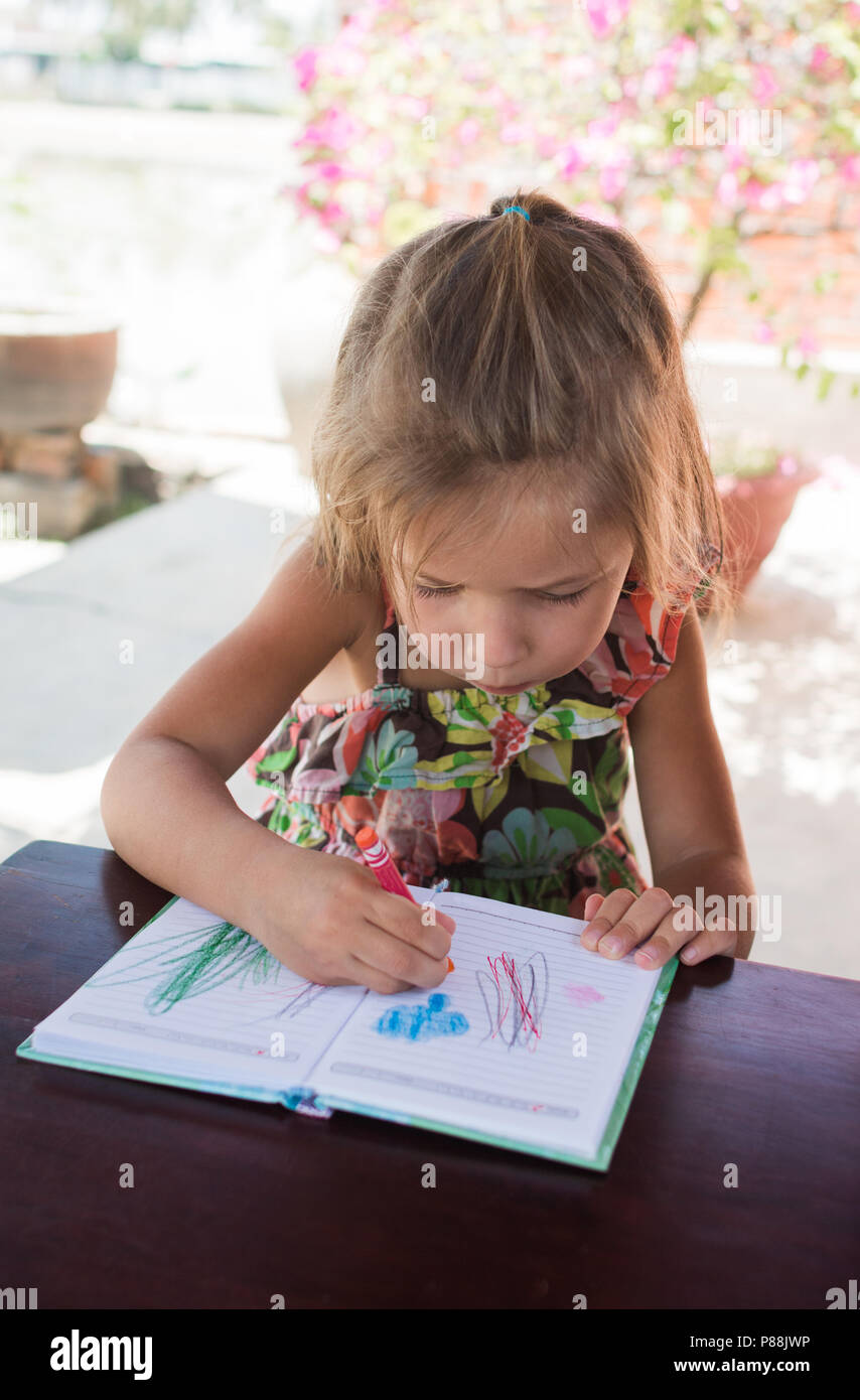 Adorable little girl drawing artwork top view on crayons in a notebook ...