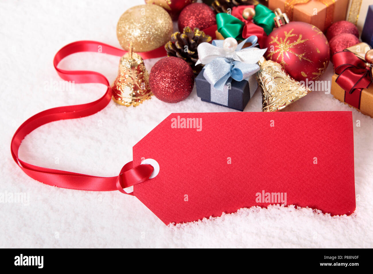 Red gift tag laying on a snow background with various gifts and ...