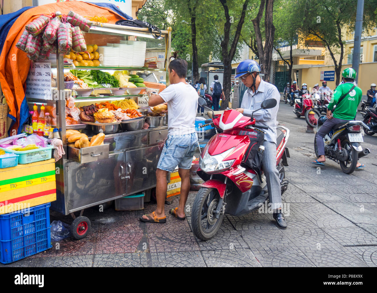 A Vietnamese man on a motorbike purchasing street food from a vendor ...