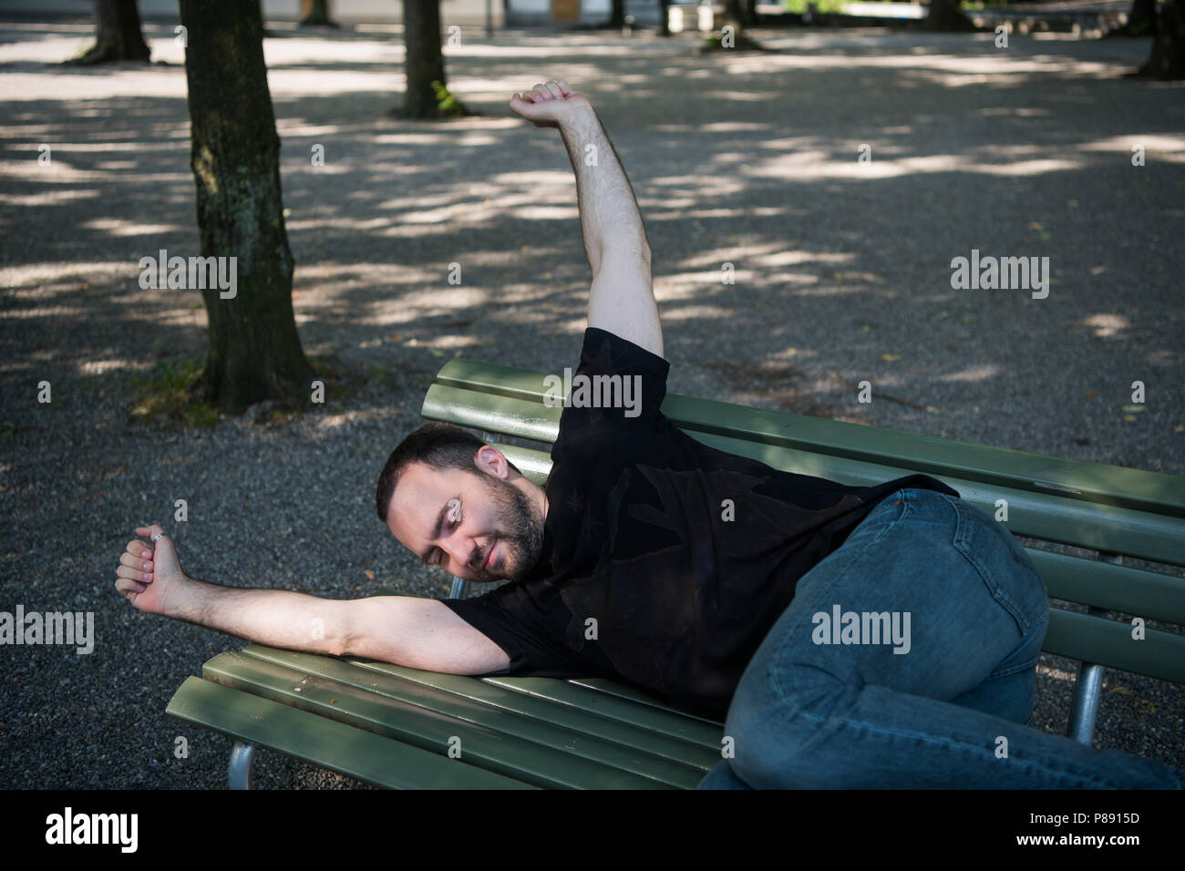 Young man lying down sleep on bench in the park and wakes up after rest ...