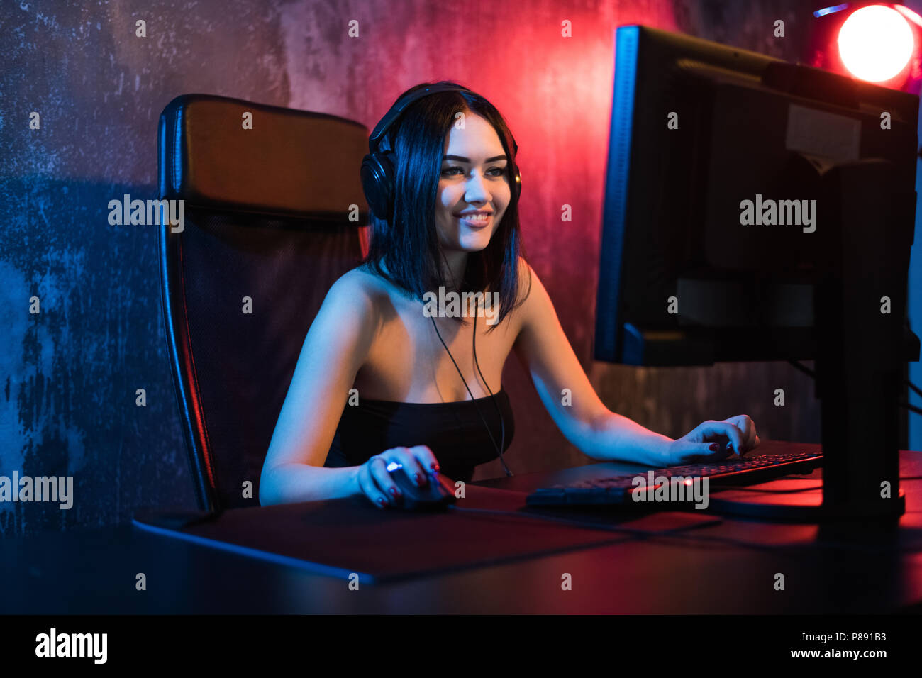 A cute female gamer girl sits in a cozy room behind a computer and ...