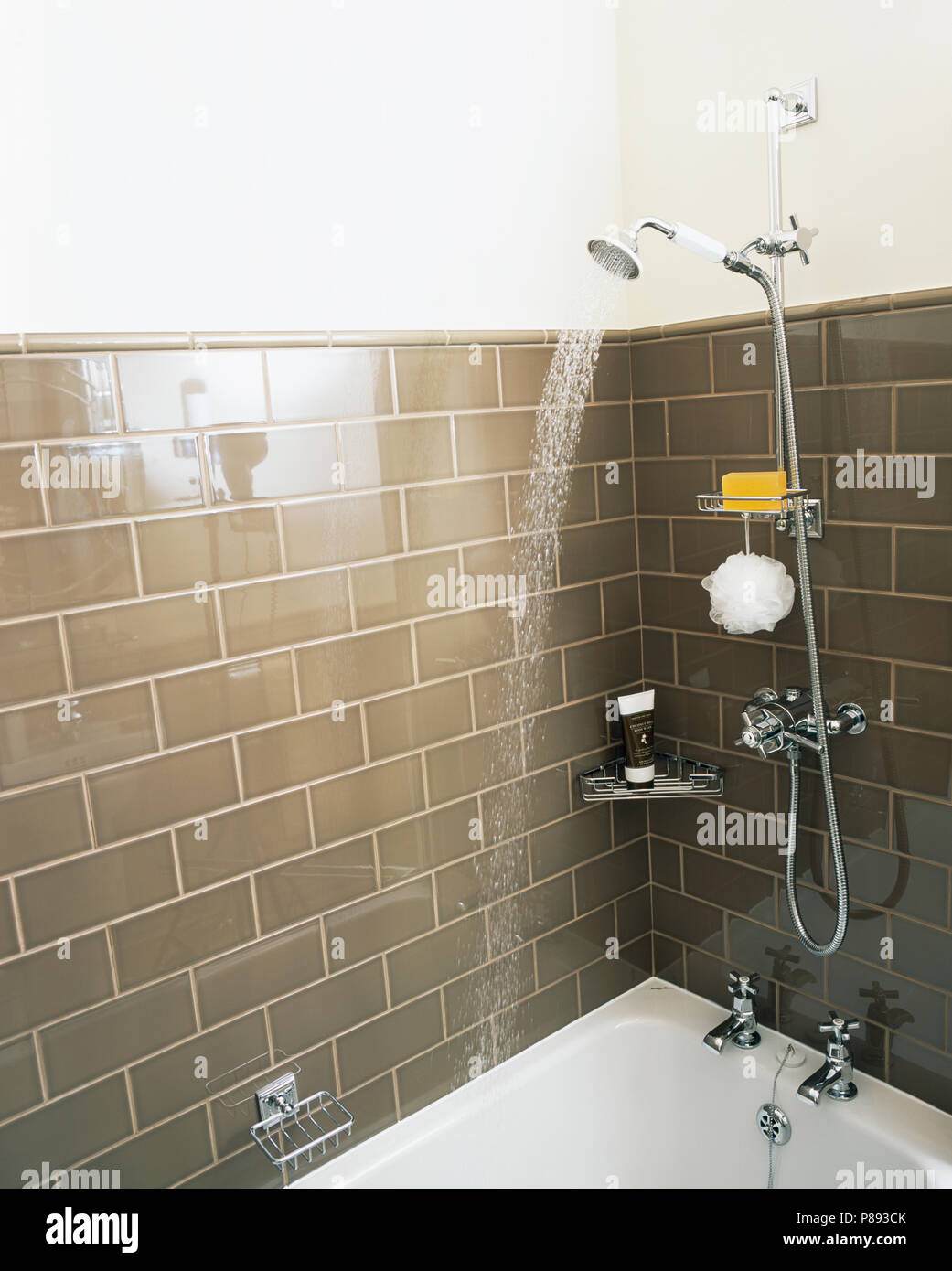 Chrome shower spraying water into bath in brown tiled townhouse ...