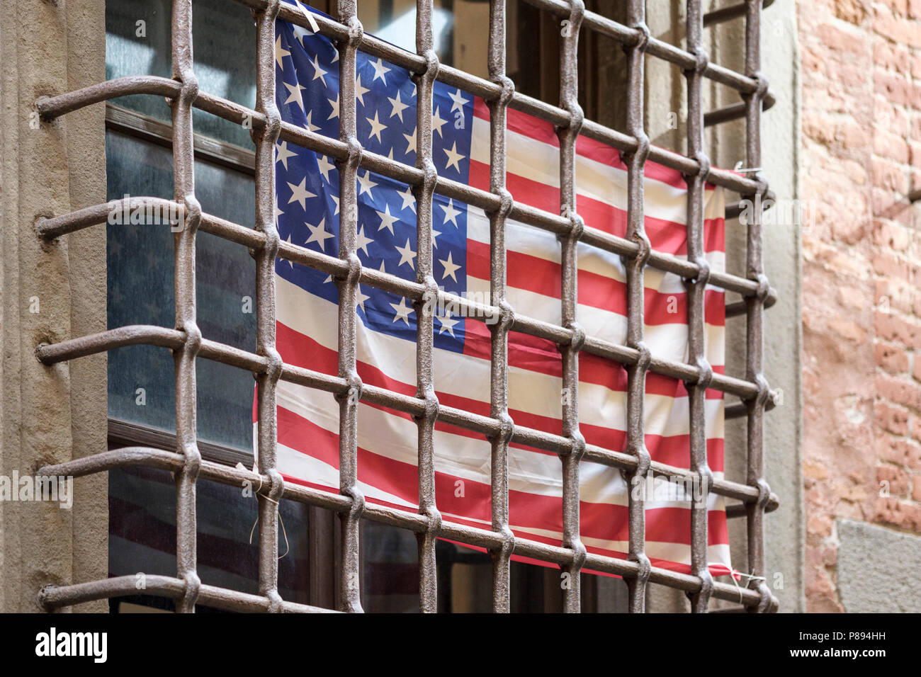American flag behind window security bars, old city street in Lucca ...