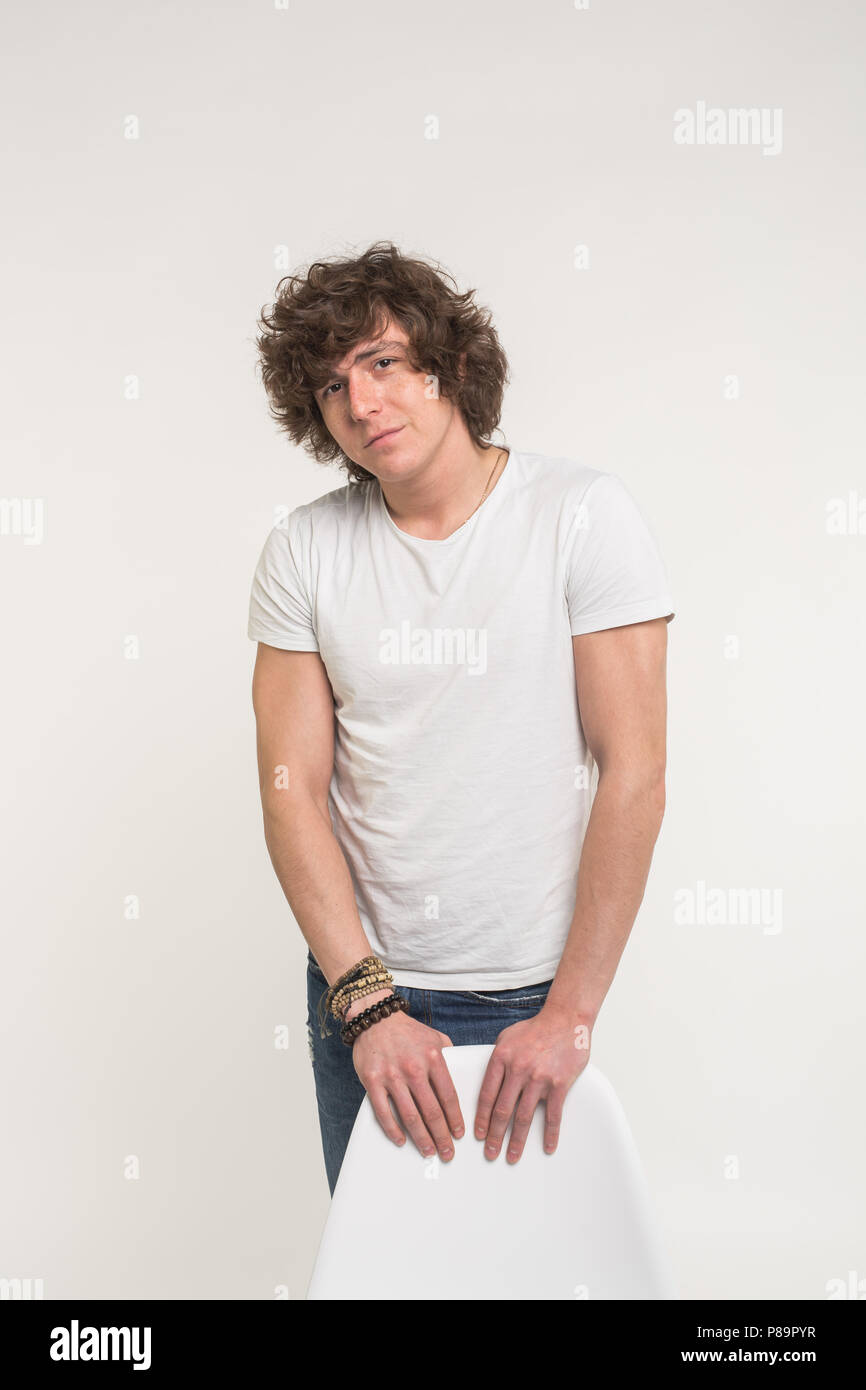 Handsome young man with curly hair standing in white t-shirt behind a ...