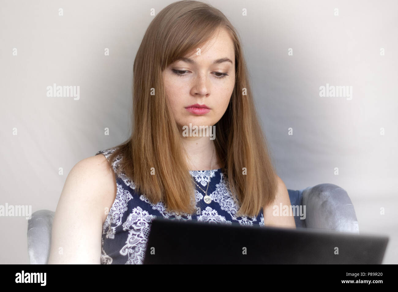 Pretty young woman with red hair wearing blue dress working on laptop ...