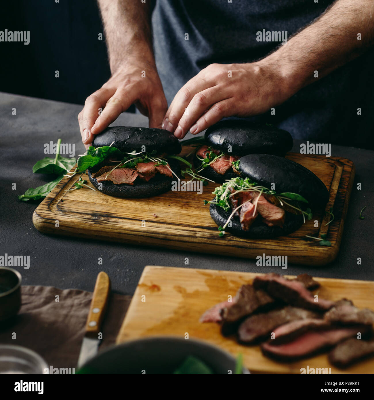 Man preparing black burgers with grilled beef meat on dark background ...