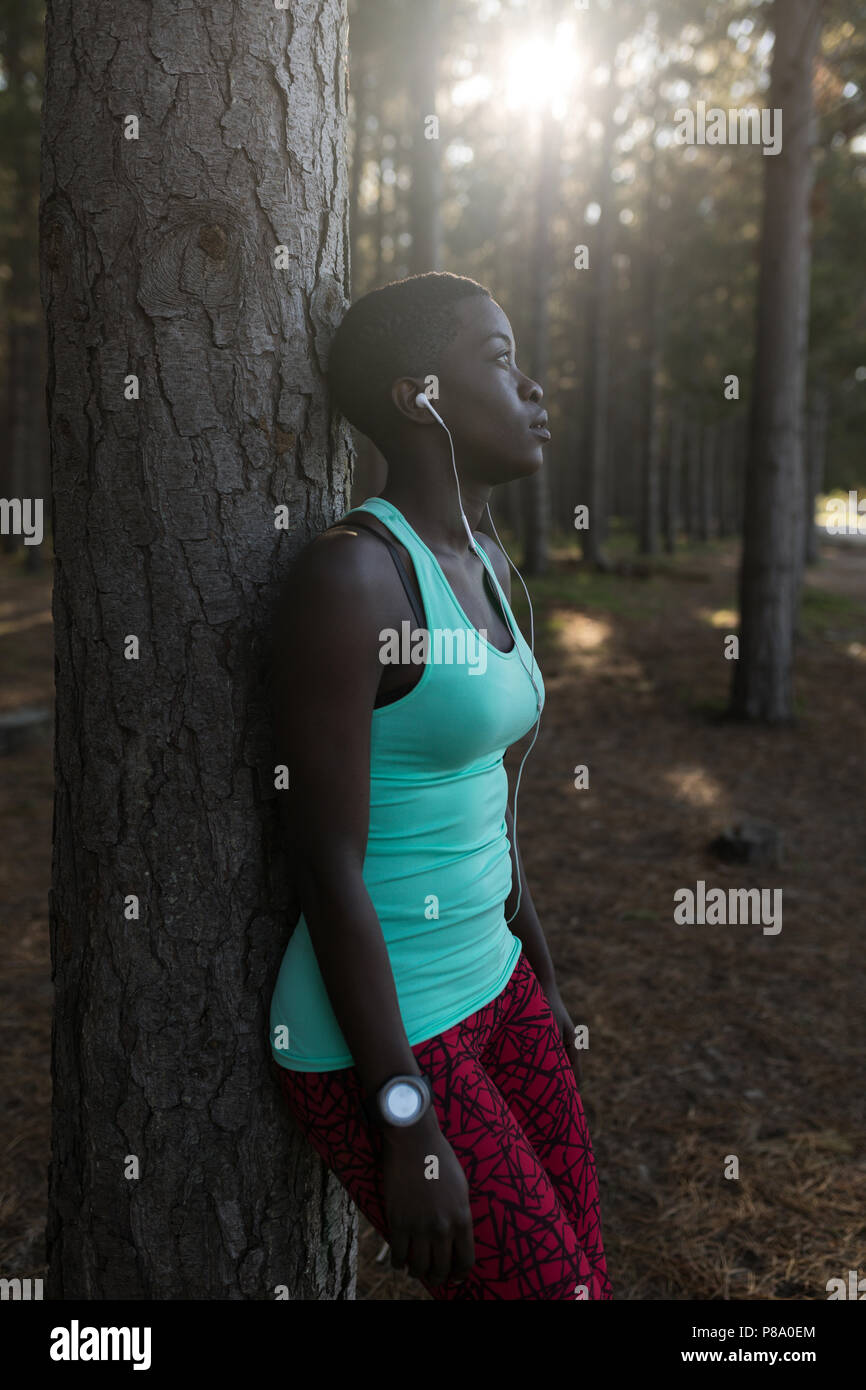 Exhausted female athlete leaning against the tree trunk Stock Photo - Alamy