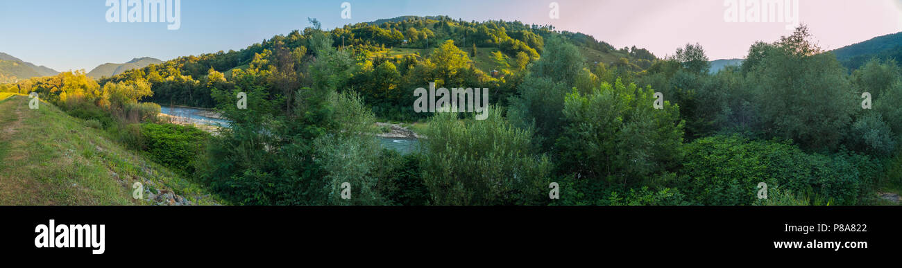 A small fast river against the background of large green hills and ...