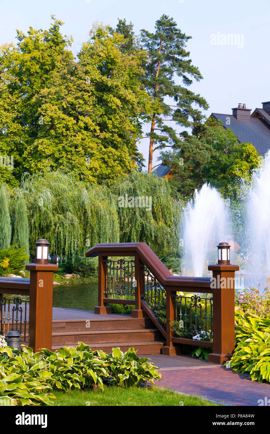 a modern wooden bridge across the lake with fountains, surrounded by ...
