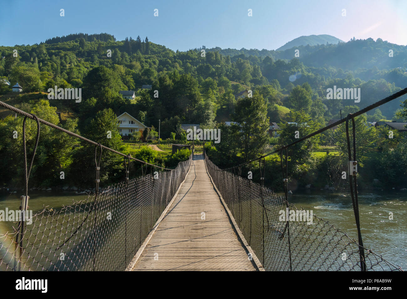 pedestrian bridge across a mountain river leading to rural houses ...