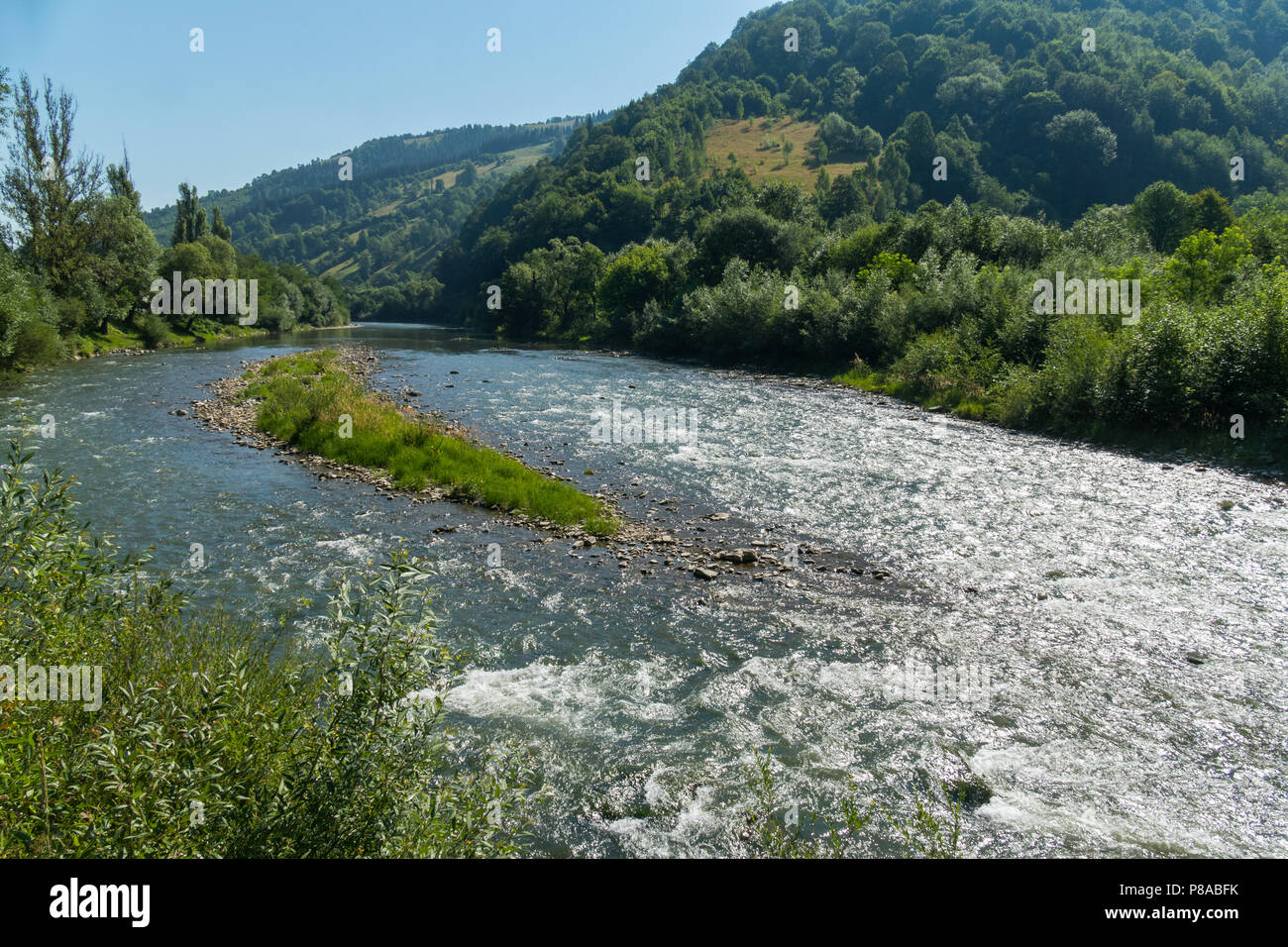 a refreshing river running at the foot of a mountain between low green ...