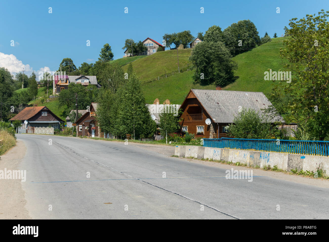 A wide asphalt road with large beautiful cottages and small rural ...