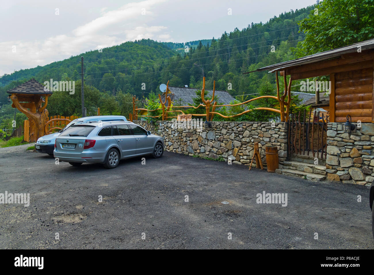 Two silver cars in a tiny parking lot with a wicker fence near a cafe ...