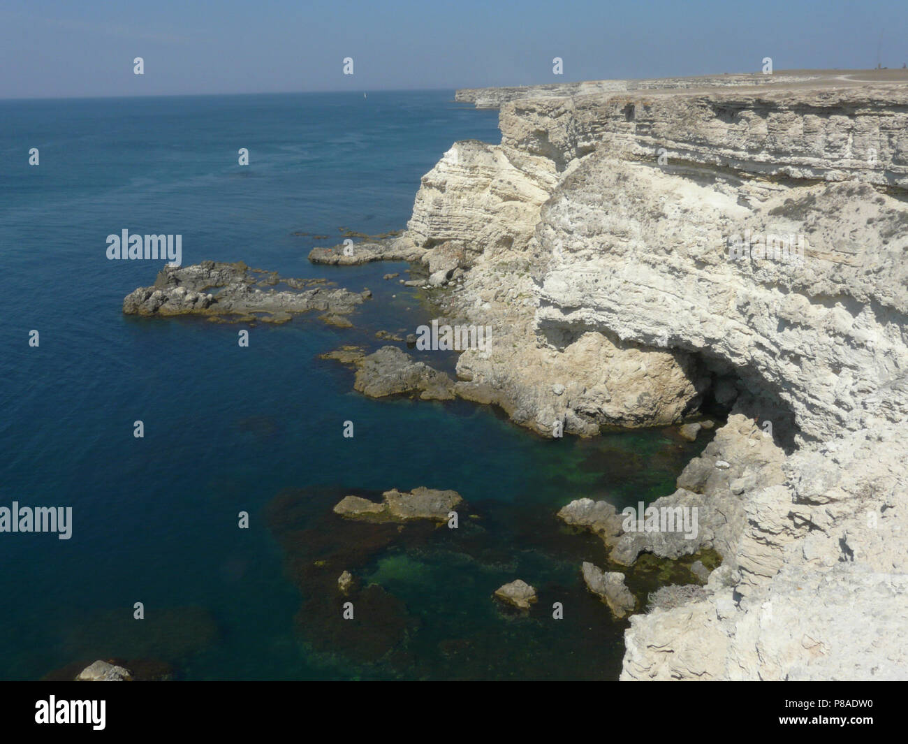 An empty, stone beach of gray rocks, with a high cliff above a deep ...