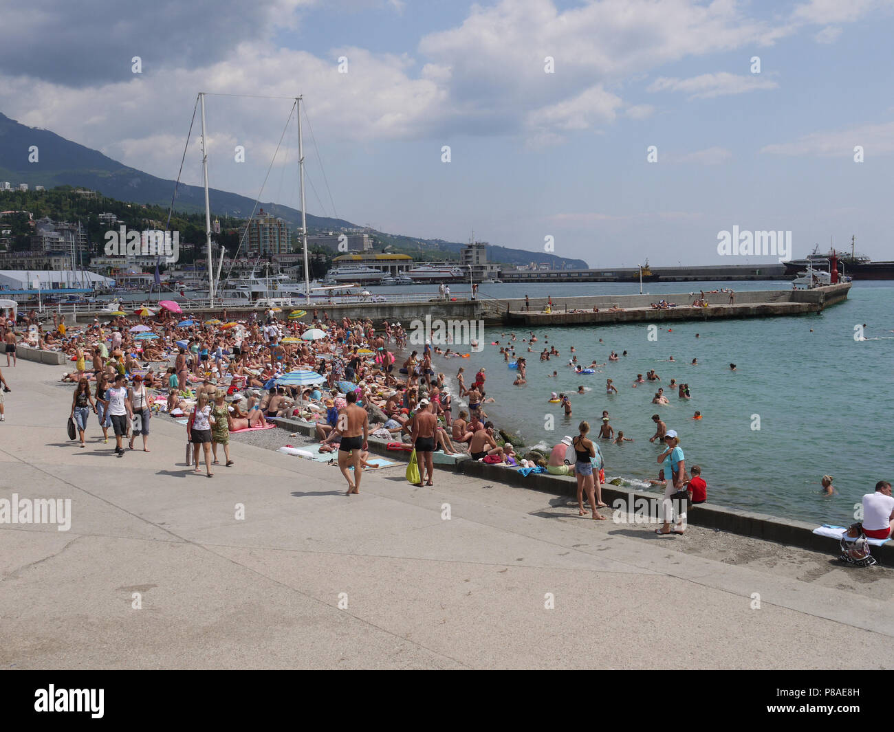 crowded resting concrete quay, beach and pier on the background of ...
