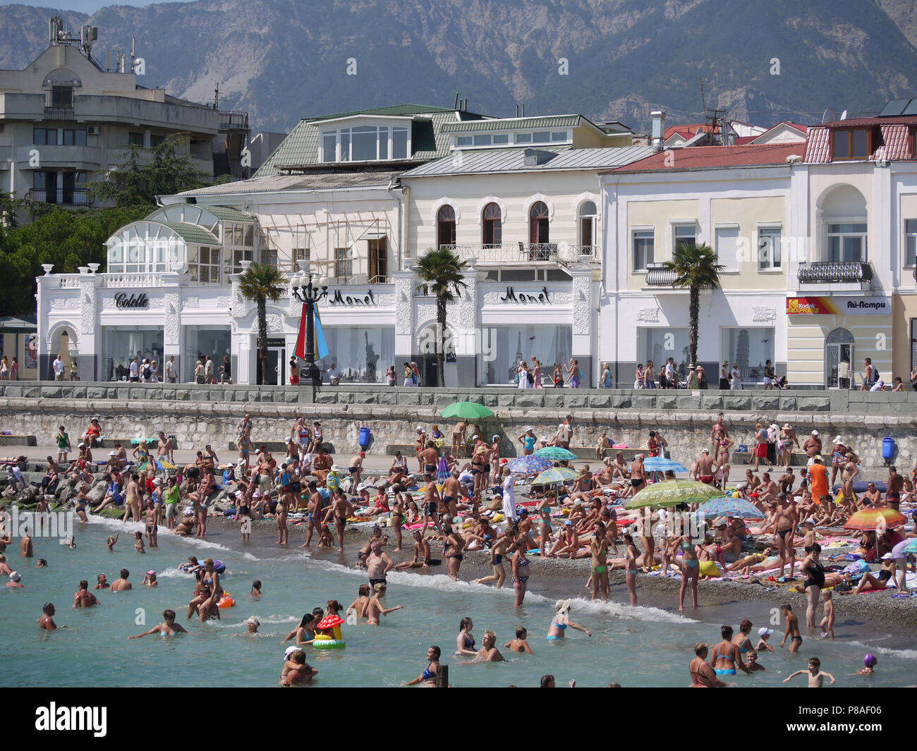 A small beach on the seashore is packed with people. In the background ...
