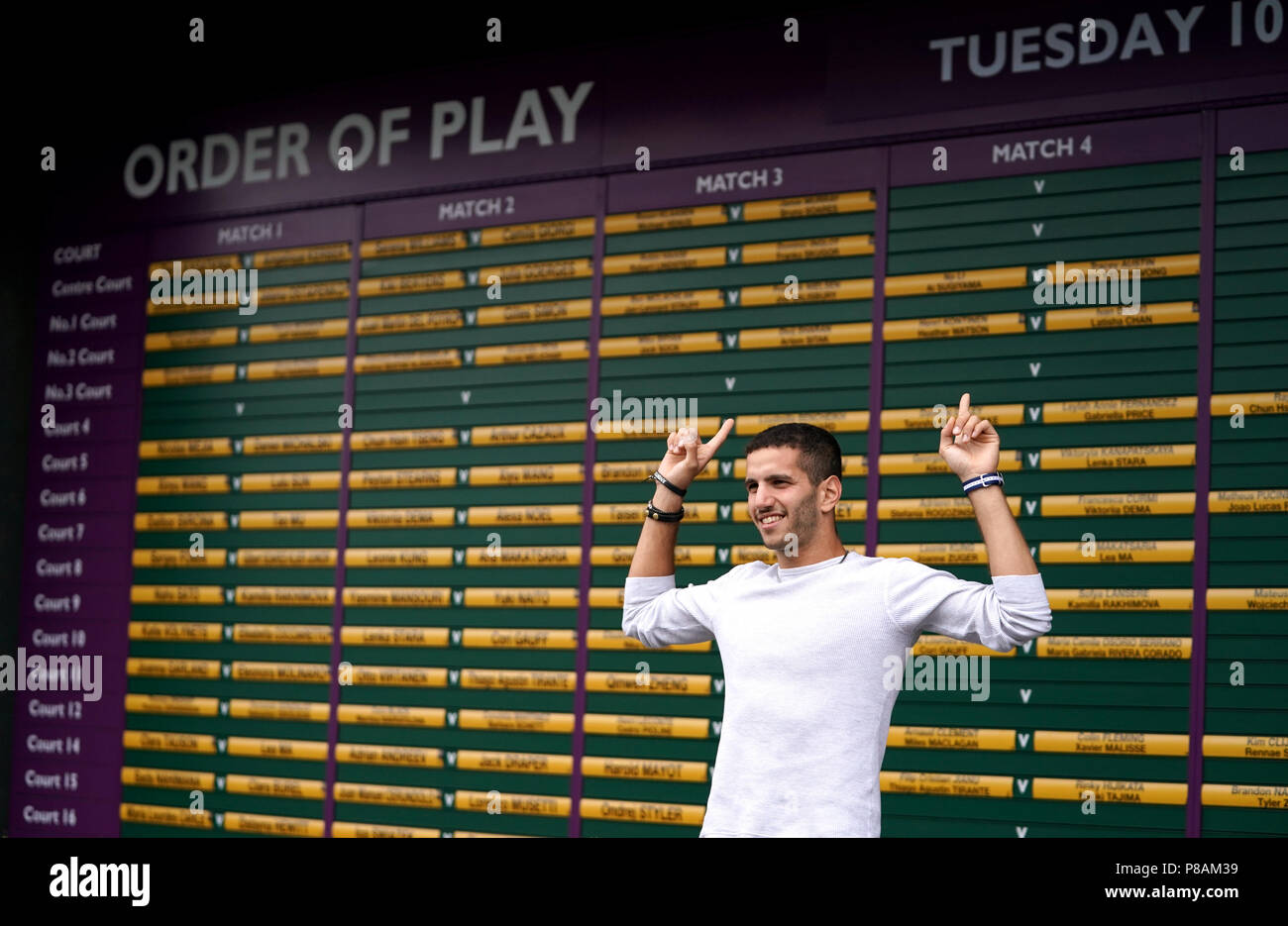 A spectator poses for a picture against the order of play board on day ...