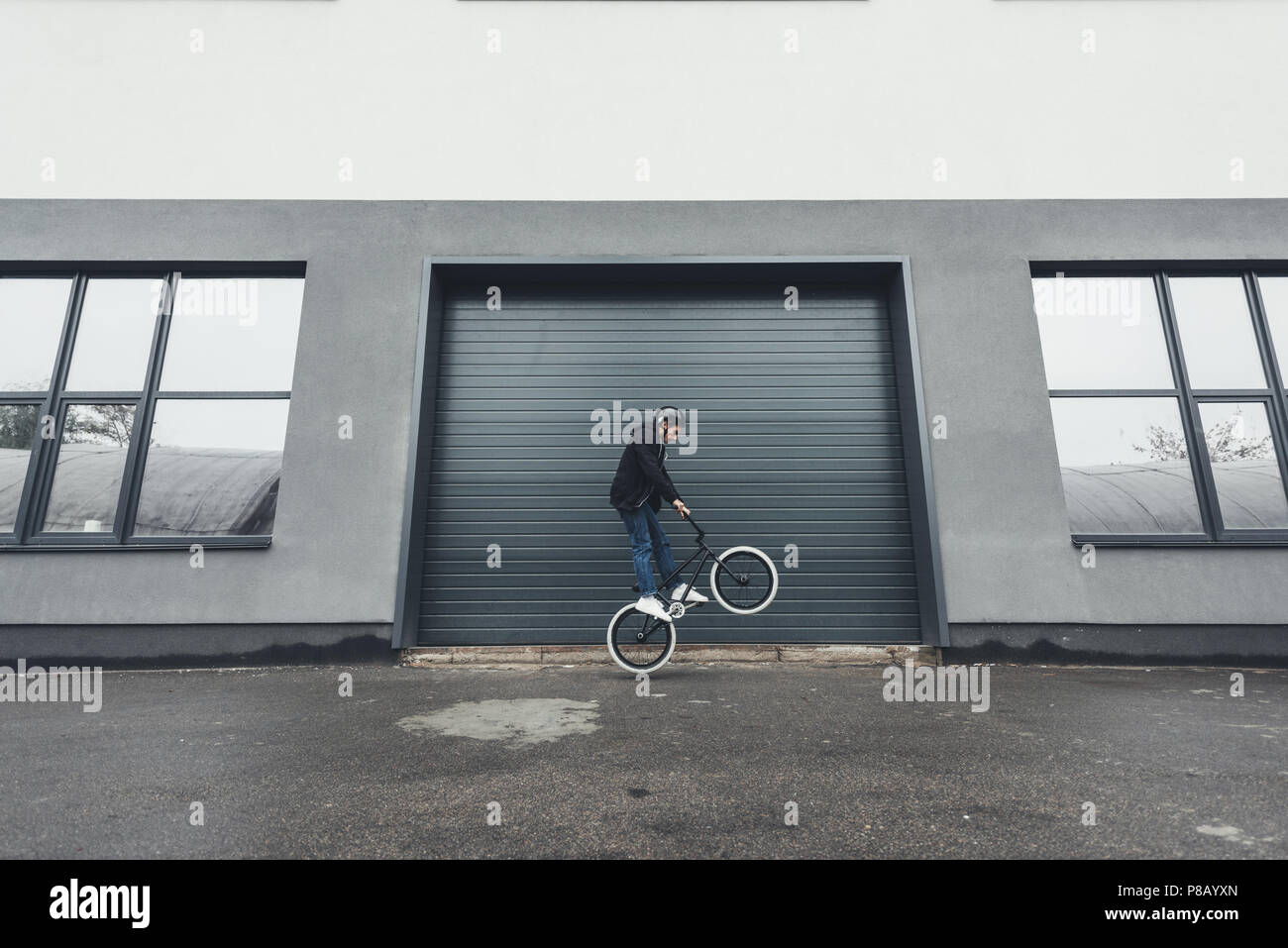 side view of young man in helmet performing stunt on bmx bicycle on ...