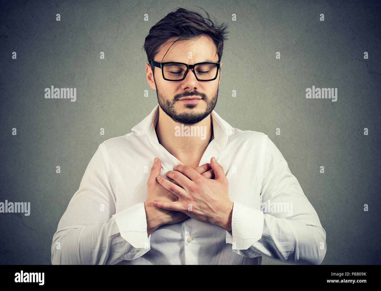 Faithful man with eyes closed keeps hands on chest near heart, shows ...