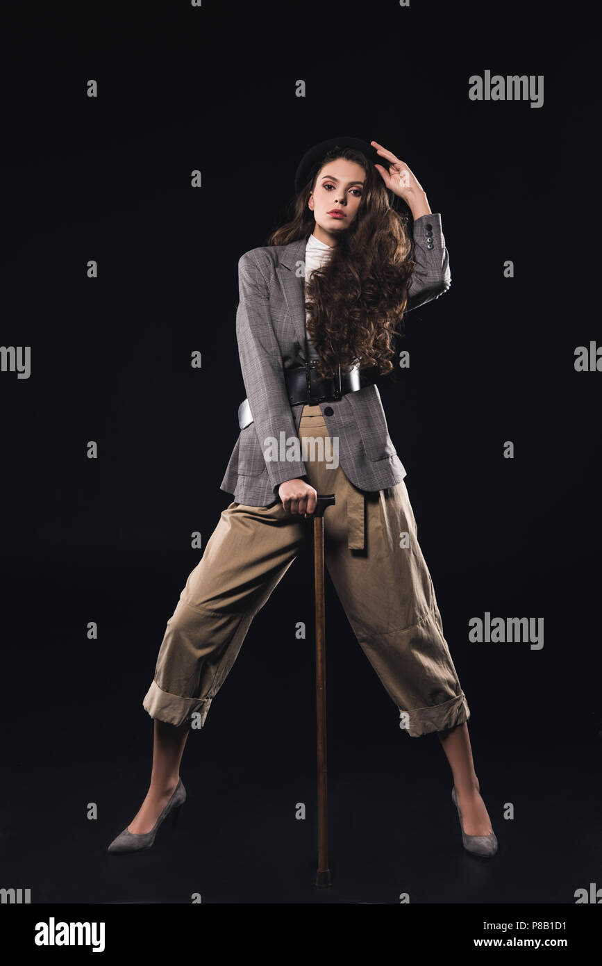 stylish young woman posing with walking stick and looking at camera ...