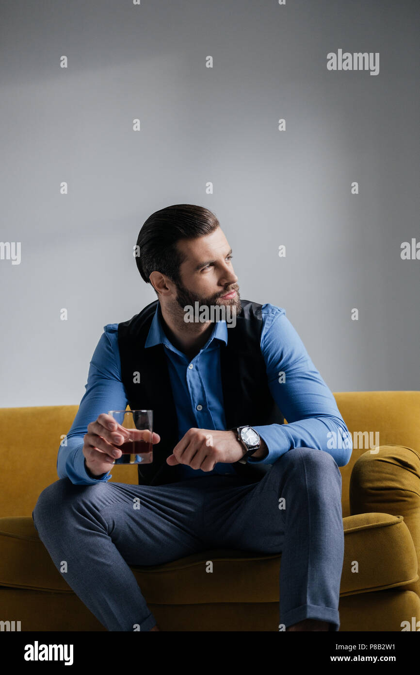 stylish man holding alcohol drink and sitting on yellow sofa Stock ...