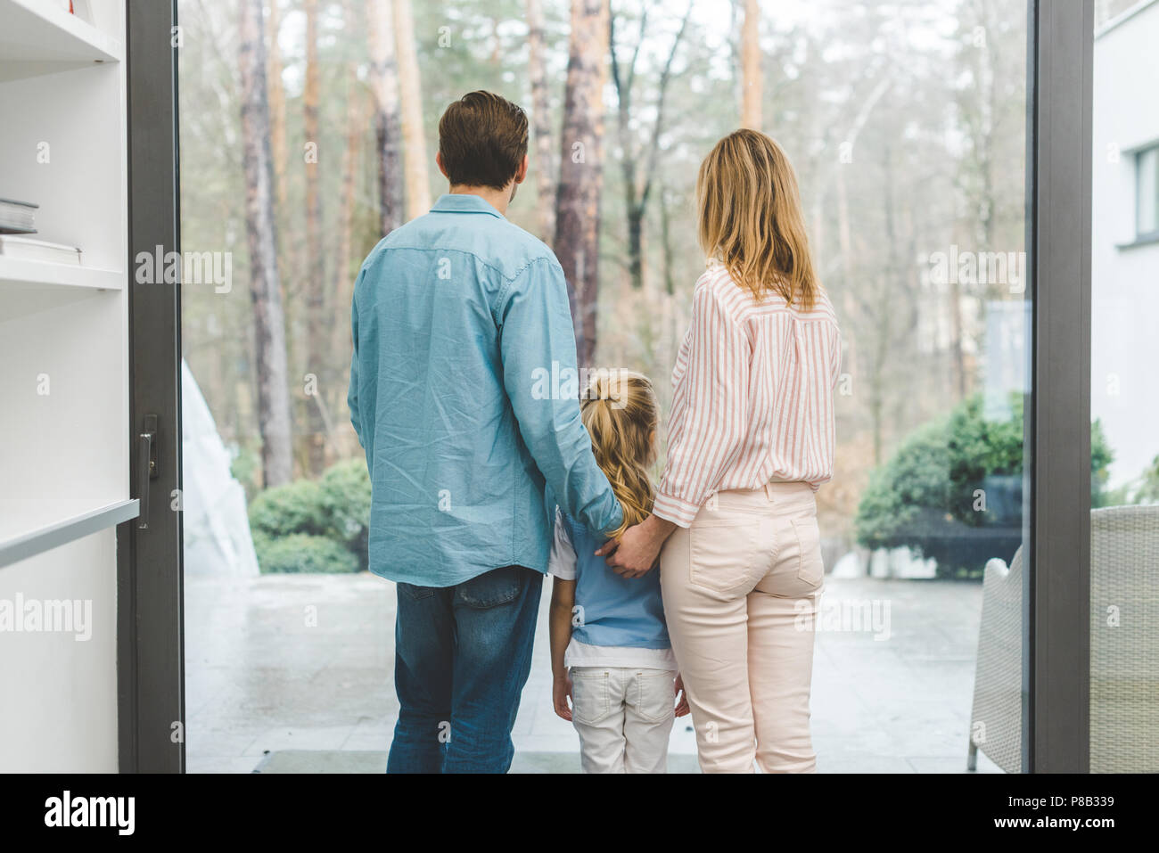 back view of family looking out window at home Stock Photo - Alamy