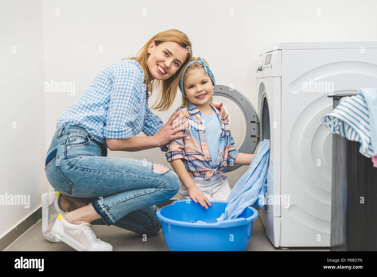 Mother And Daughter Looking At Camera While Putting Clothes Into