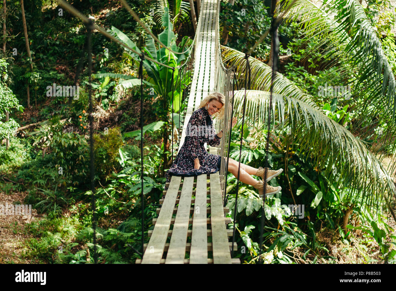 smiling attractive woman sitting on wooden footbridge in jungle Stock ...