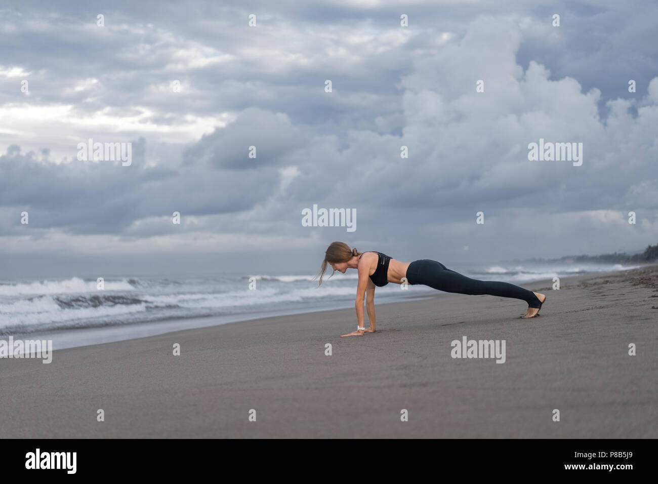 side view of young woman practicing yoga in plank pose on seashore ...