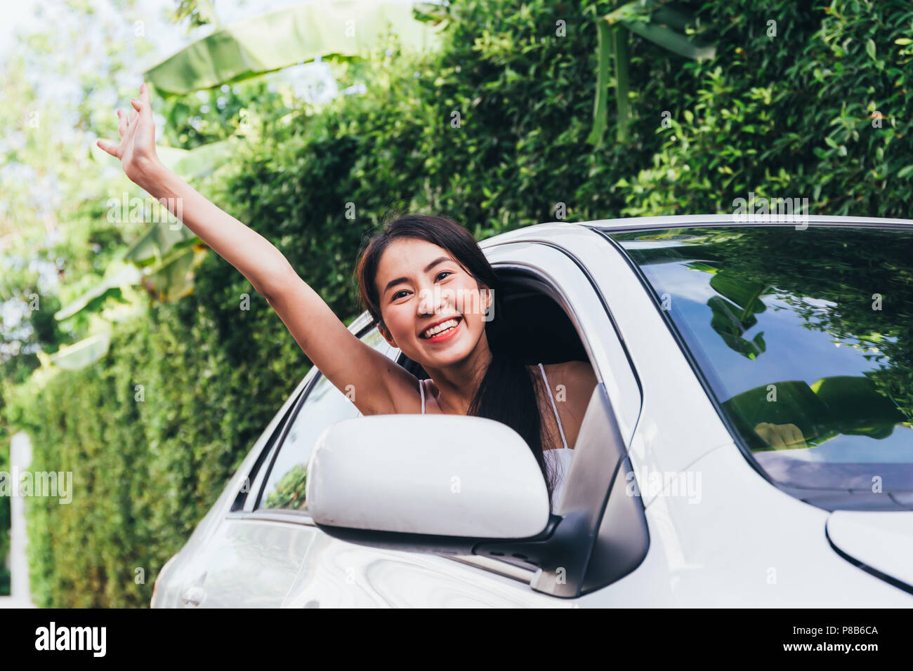 Young Happy Asian woman smiling and waving from drivers seat in car ...