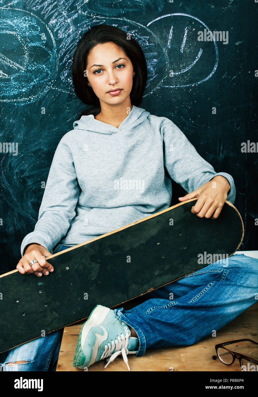 young cute teenage girl in classroom at blackboard seating on table ...