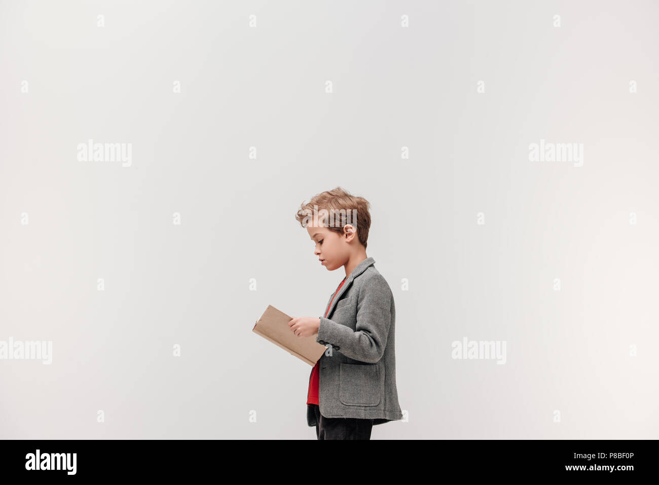 side view of stylish little schoolboy reading book isolated on grey ...