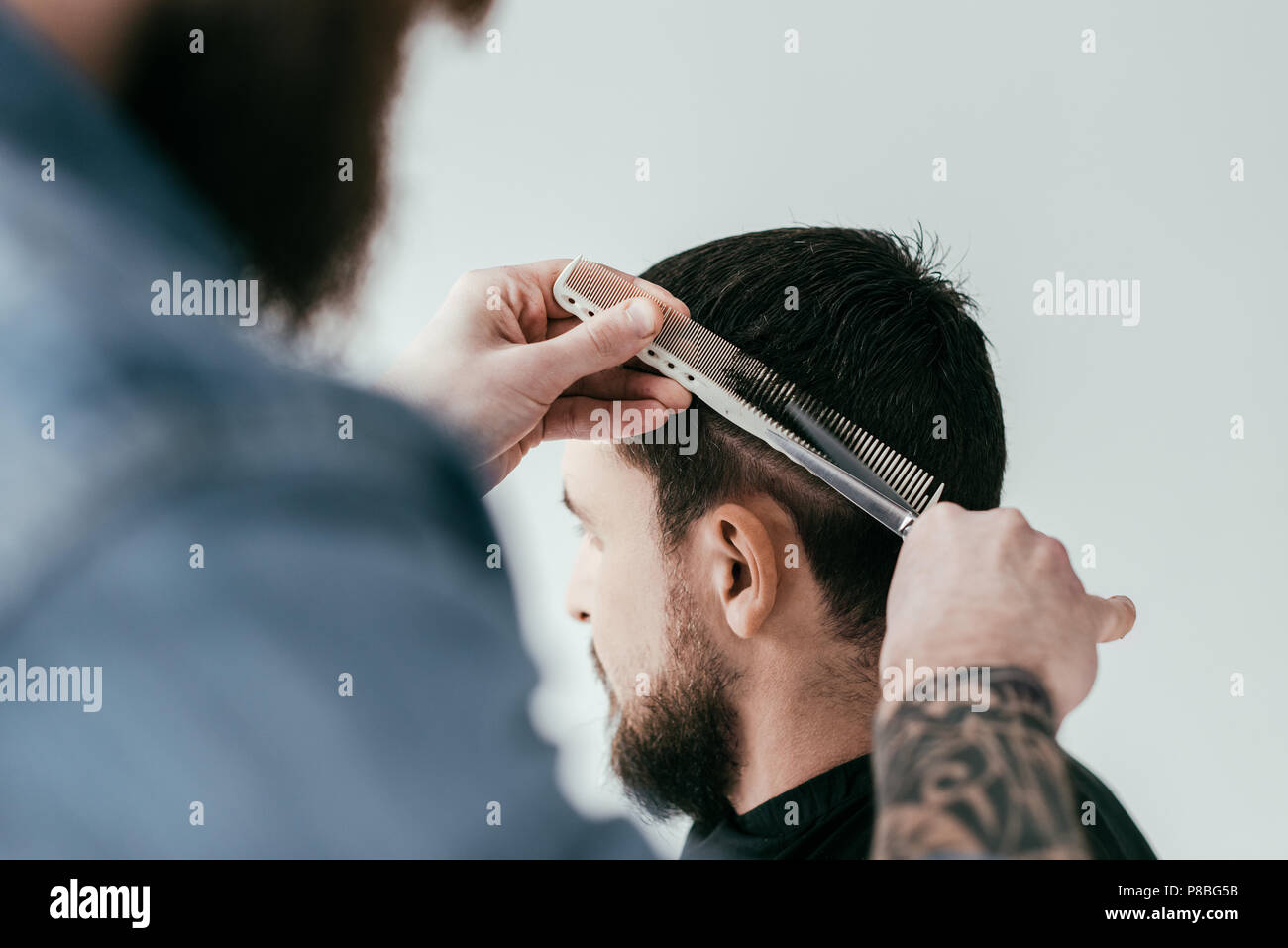 cropped image of barber cutting customer hair with scissors and comb at ...