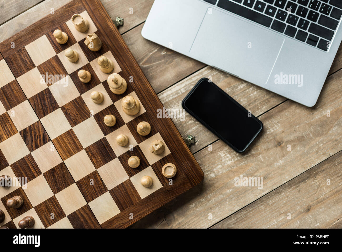 Smartphone, laptop and chess board with chess pieces on wooden surface ...