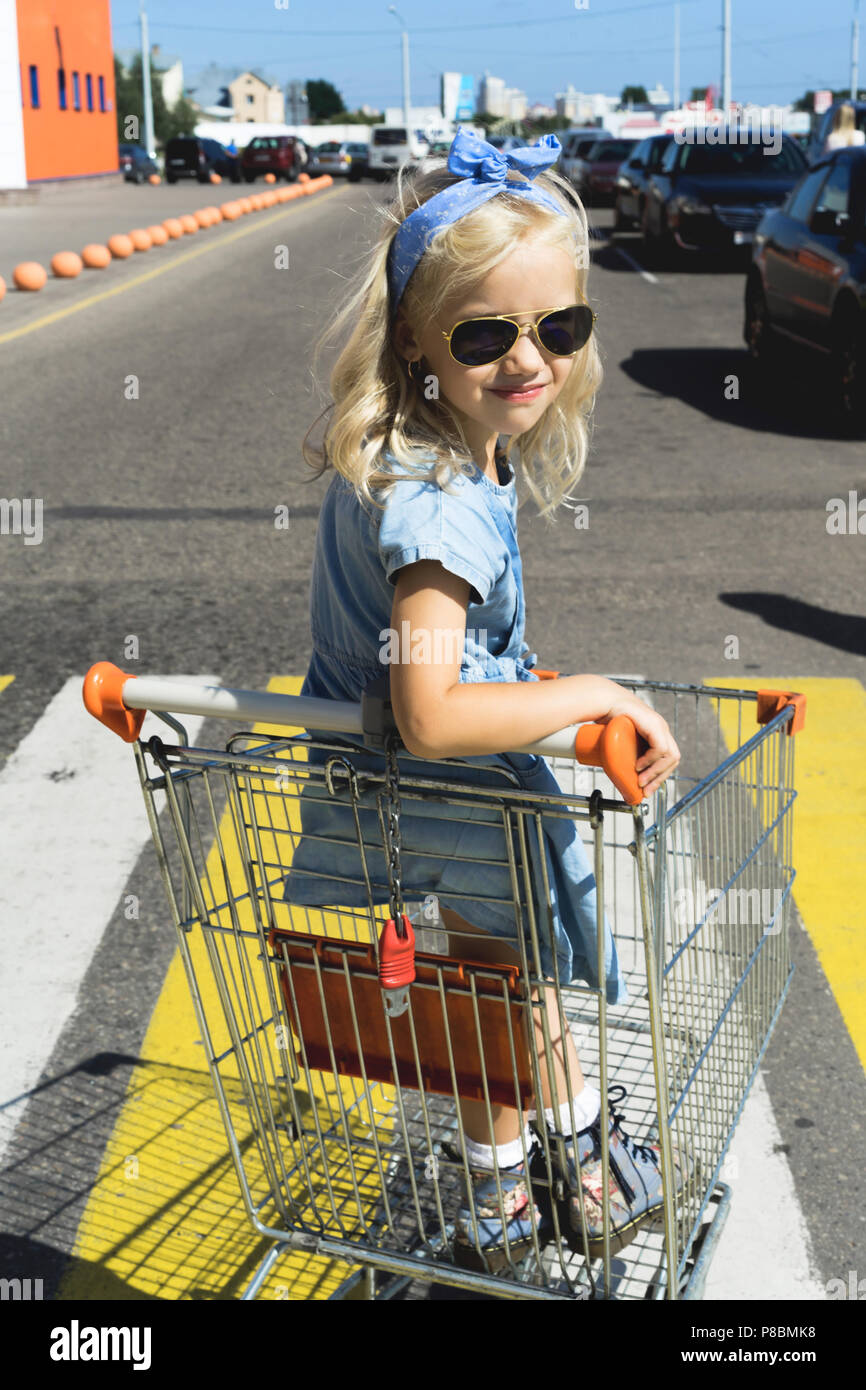 little adorable female child having fun in shopping cart at parking ...