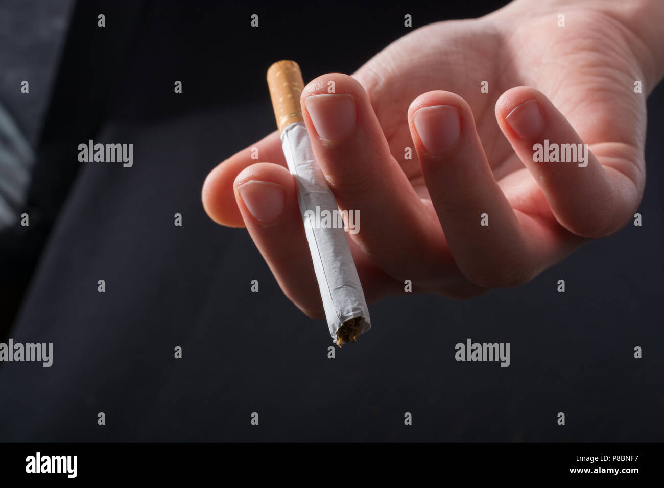 Hand is giving out cigarette on a black background Stock Photo - Alamy