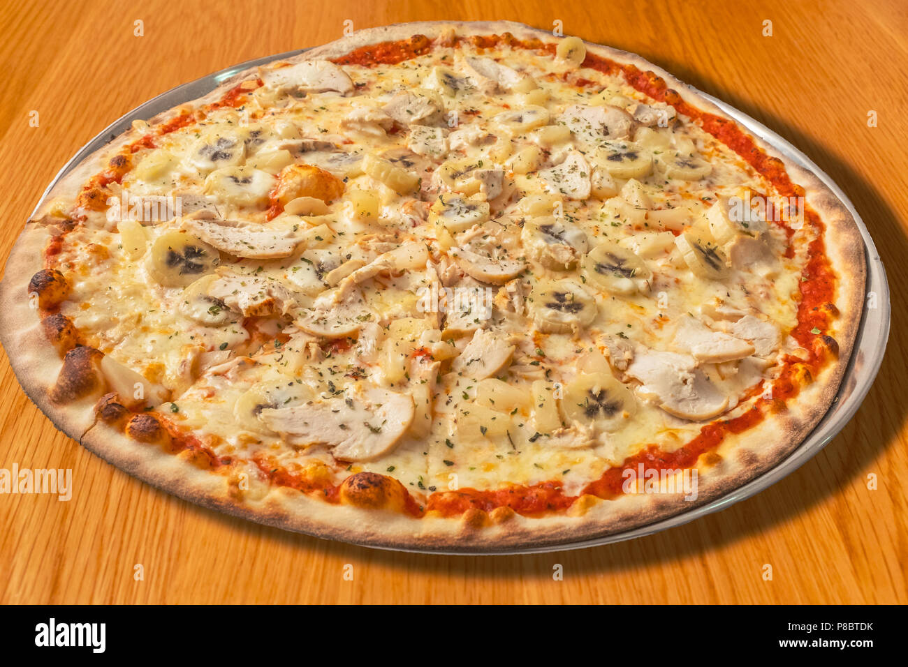 large round pizza with unusual toppings of chicken, banana, pinapple ...