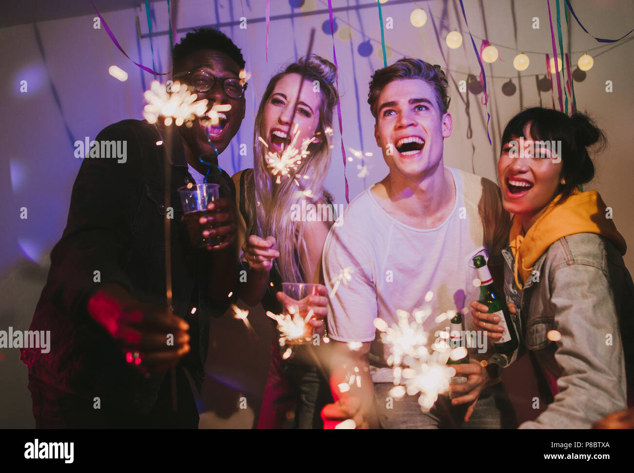 Friends celebrating with fire sparkles and drinks at a house party ...