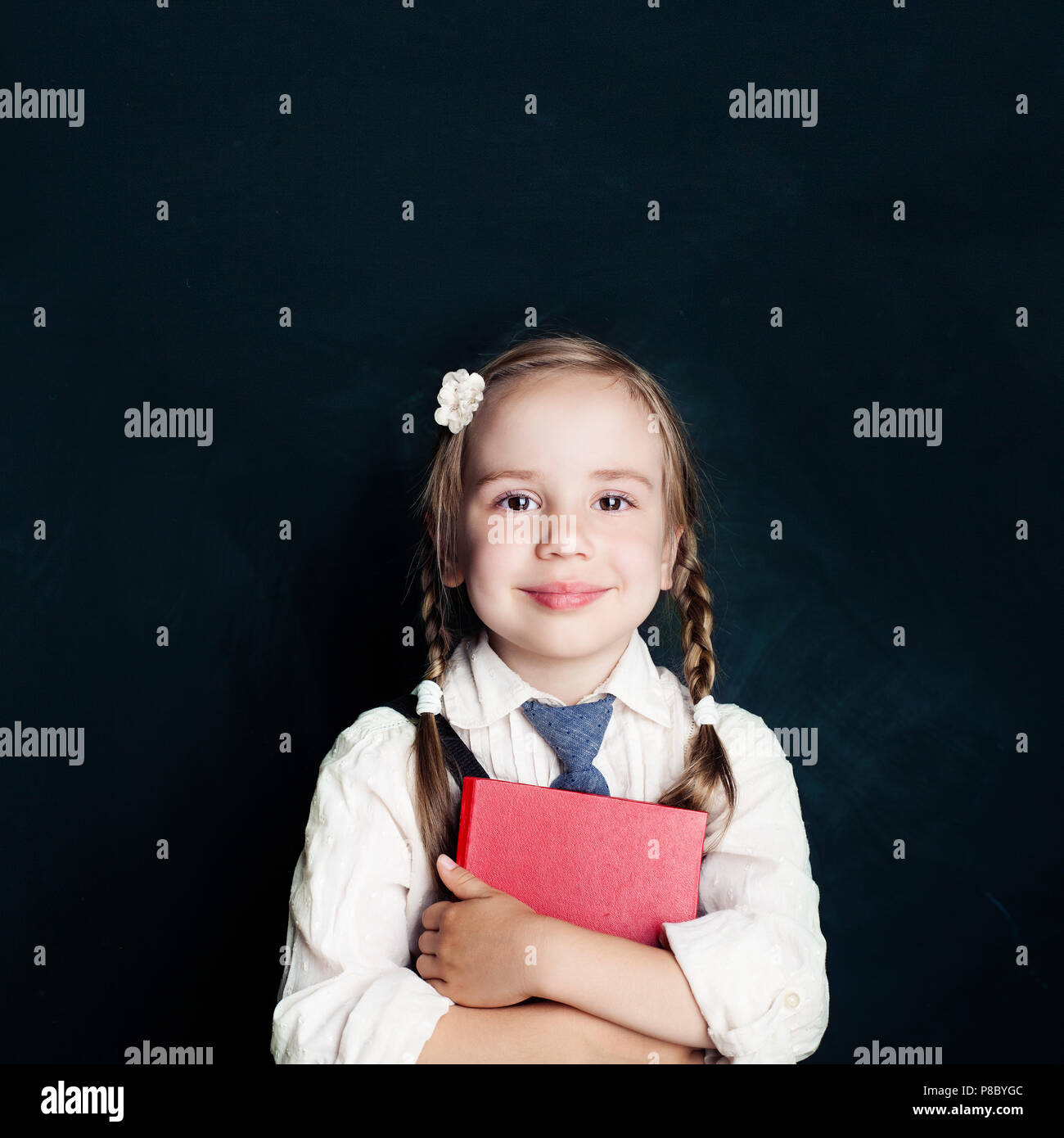 Happy little girl with red school book on a blackboard background. Kid ...