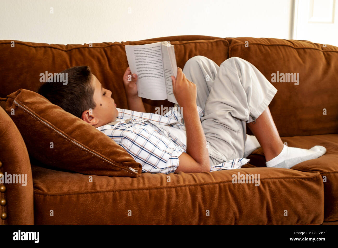 Boy reading book on sofa in family room. MR © Myrleen Pearson ...