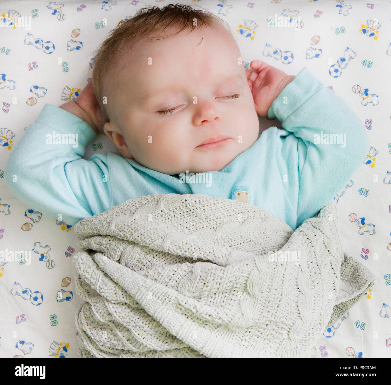Infant laying on his back on a bed with his hands up near his head ...
