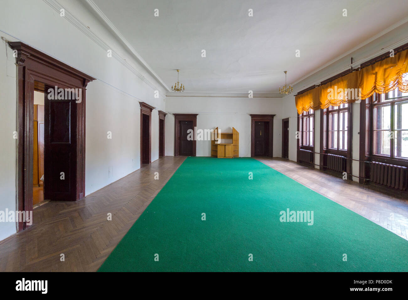 A wide corridor is conduced by a green path and parquet with many doors ...