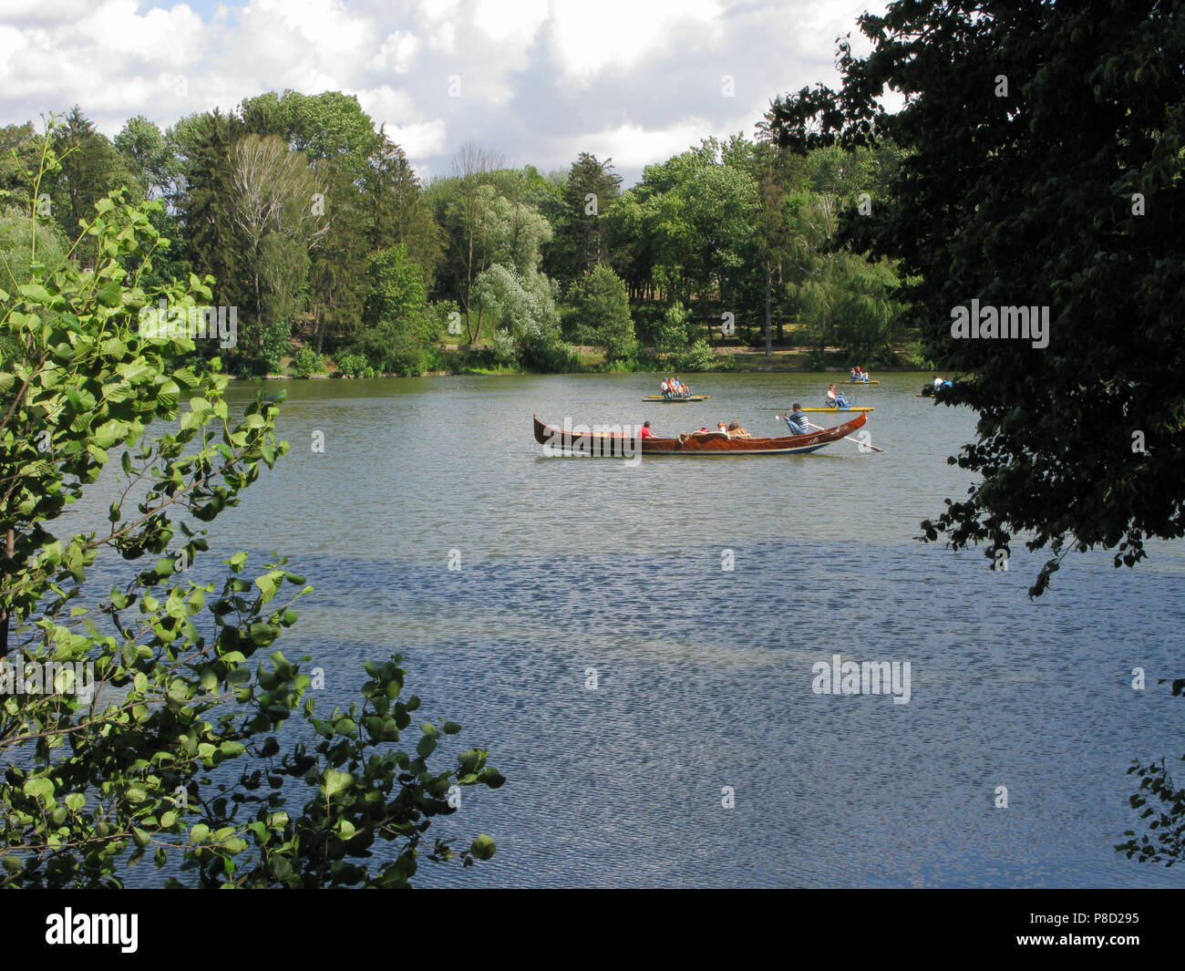 A sunny warm day in the park with people skating along the lake on ...