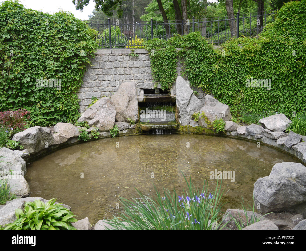 A round, small pond surrounded by stones, with a small waterfall . For ...