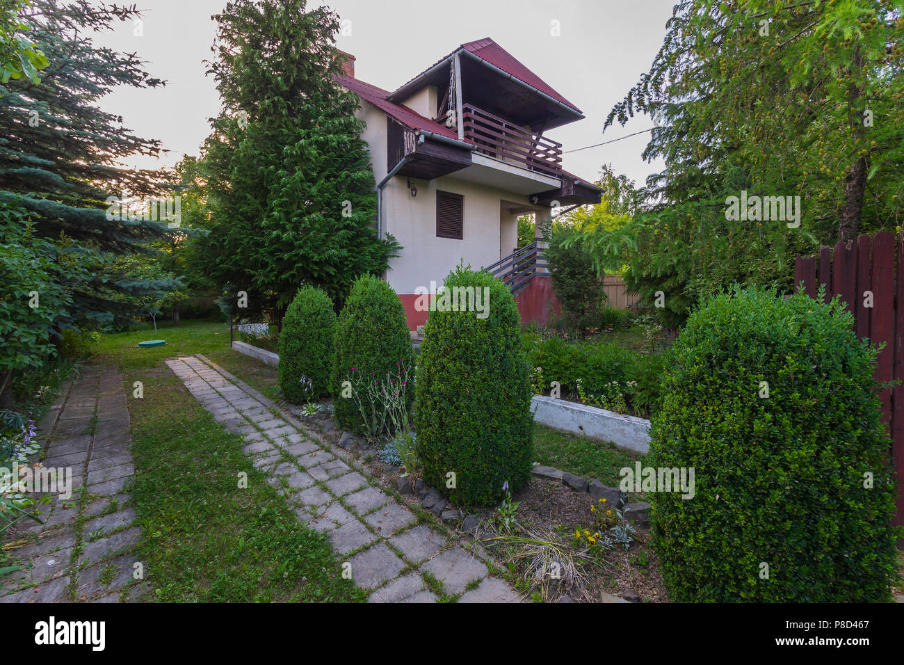 Two-storey white building with red socle and roof. Green bushes grow ...