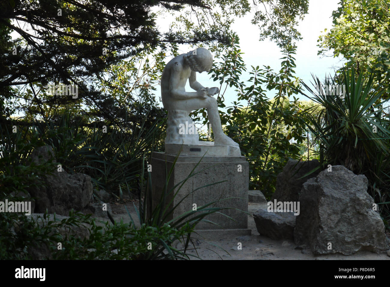A gypsum white color statue in the shade of a tree among the bushes. It ...
