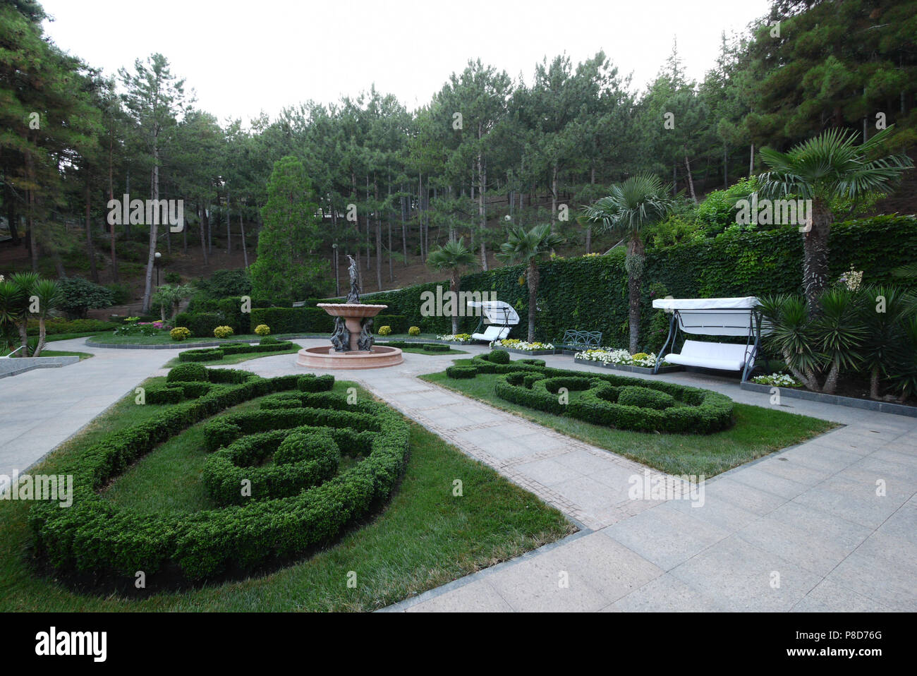 Cozy park area with a fountain, palms, swings and decorative lawns ...