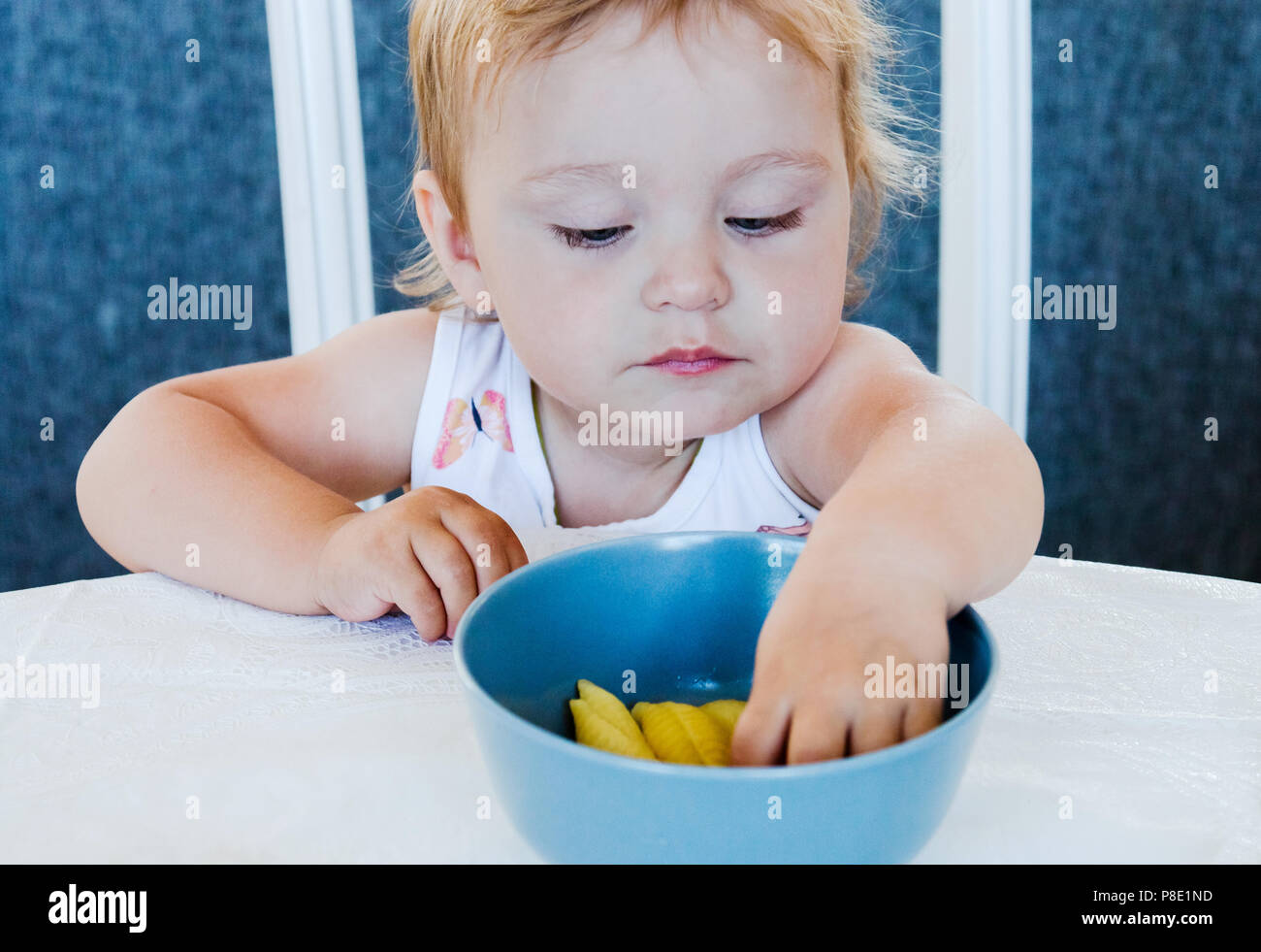 little cute blonde blue-eyed girl eating pasta with hands Stock Photo ...