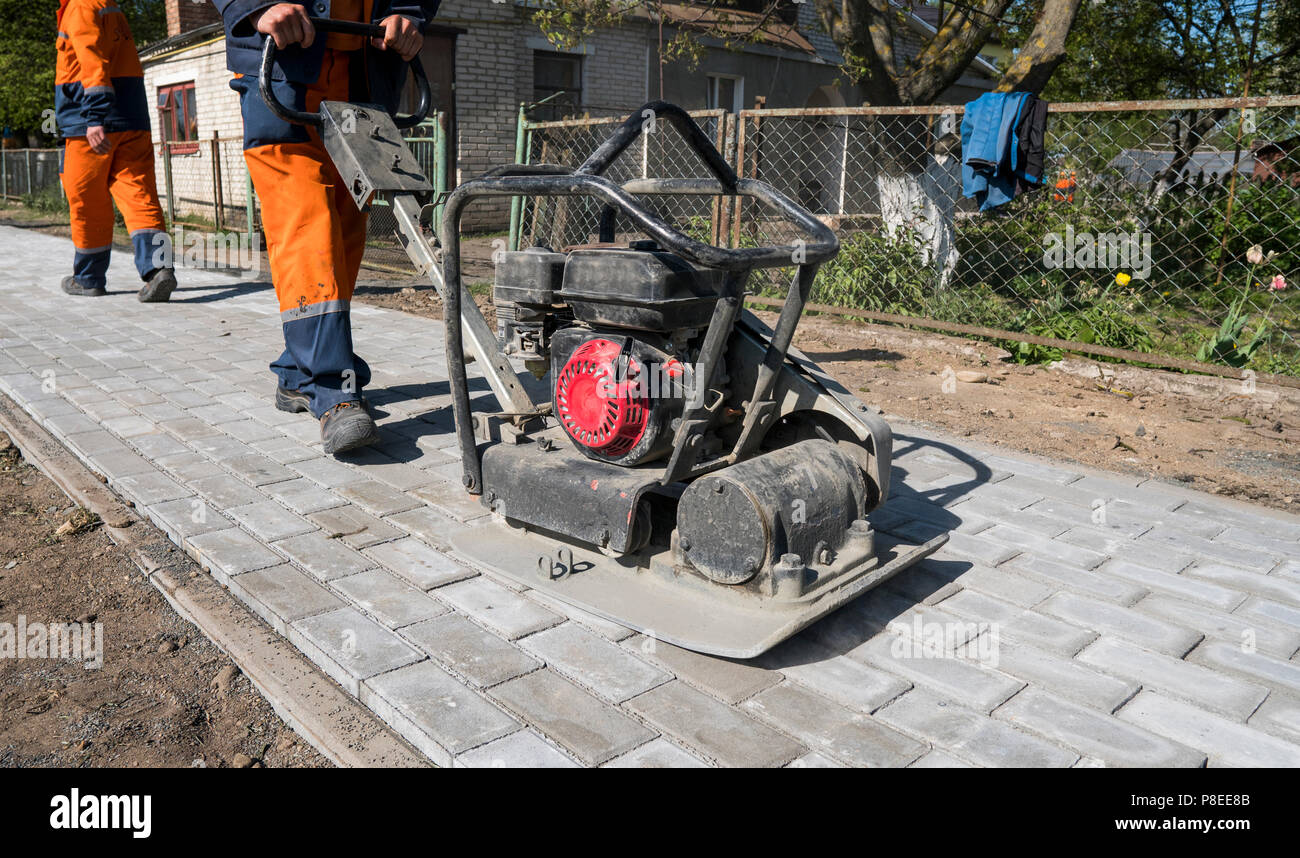 Man in orange uniform using vibrational paving stone machine for finish ...