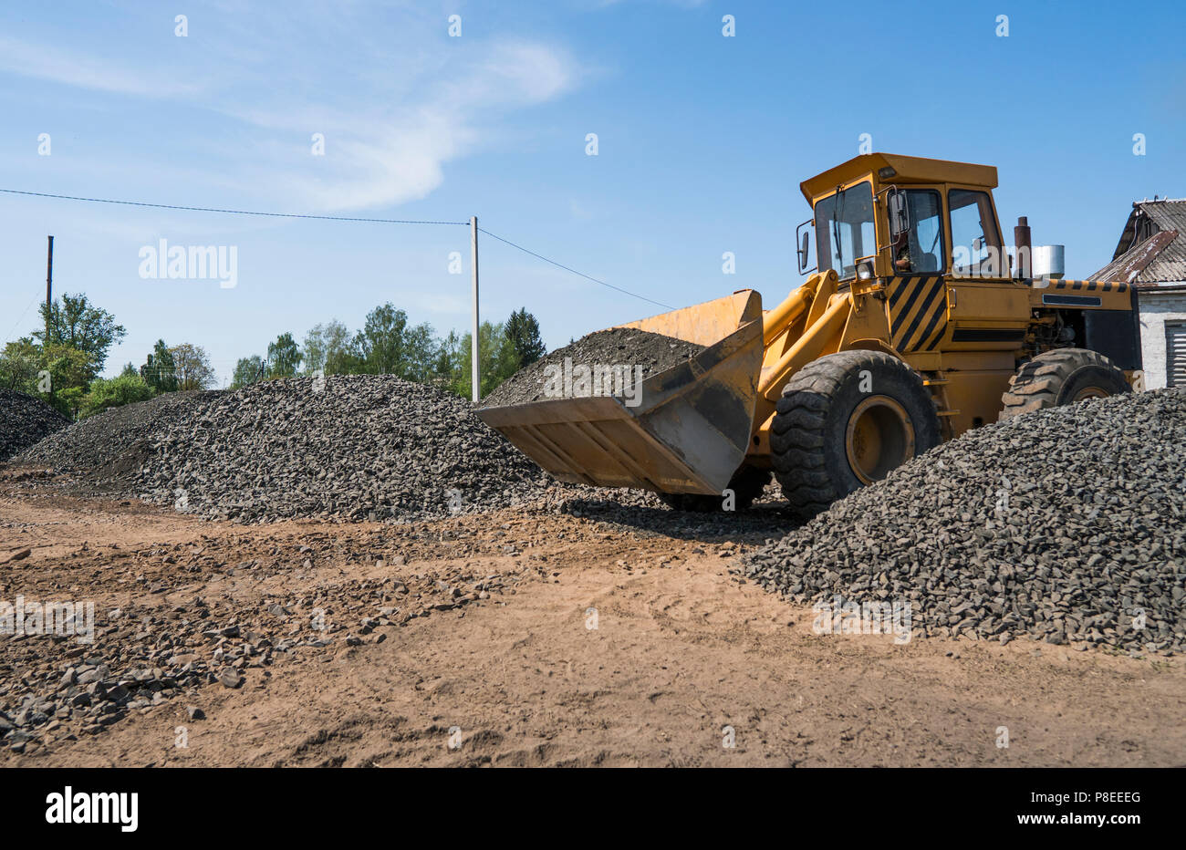 Yellow loader moving with uploaded bucket with stone gravel during road ...